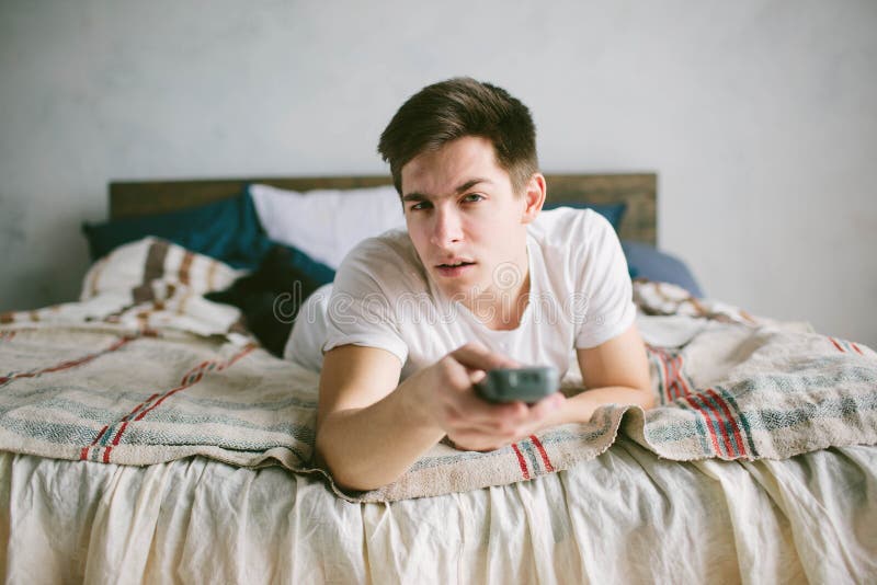Guy Using Remote Control while Sitting on the Bed in Home. Happy ...