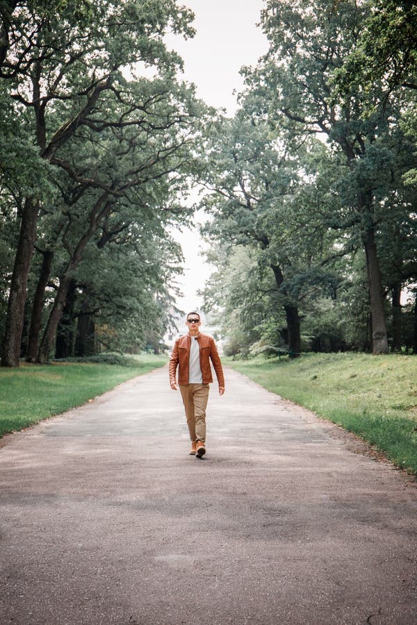 A Handsome Guy is Walking Along a Wide Road with Huge Trees, Back View ...