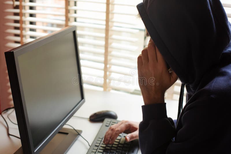 A Hacker in a Hooded Sweatshirt with a Hidden Face Typing on a Computer ...