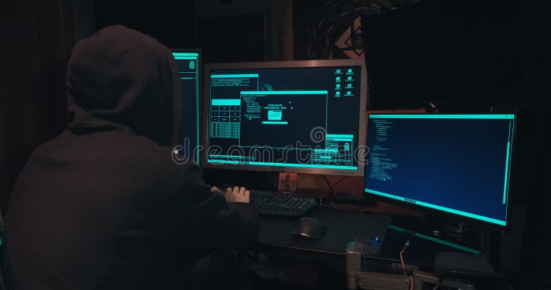 Hacker in a Hood Sits in Front of Computer Screens and Hacks Databases ...