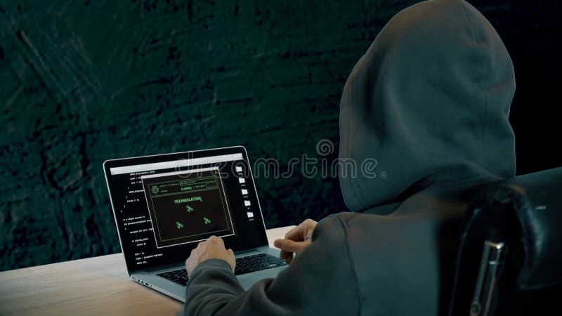 Hacker Sits at Table in Room with Concrete Walls. Man in Hood Typing on ...