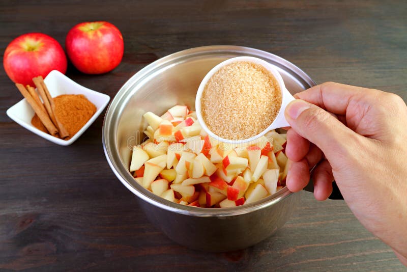 Hand Adding a Cup of Unrefined Sugar into the Pot of Diced Fresh Apples ...