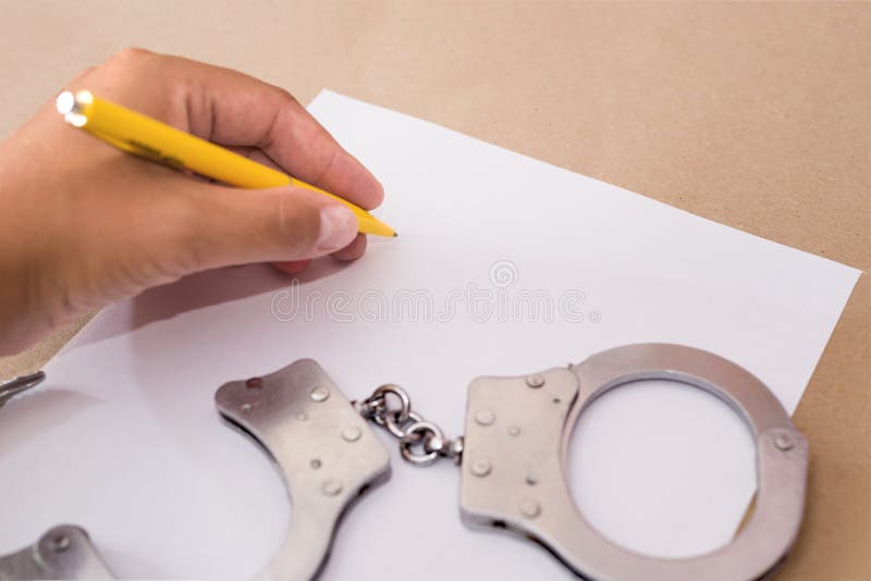 A Hand in Handcuffs Sits at a Table in Front of a Blank Sheet of Paper ...