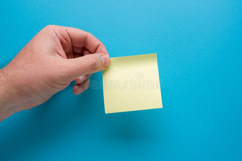 Hand Holding Blank Yellow Post-it on Blue Background Stock Image ...