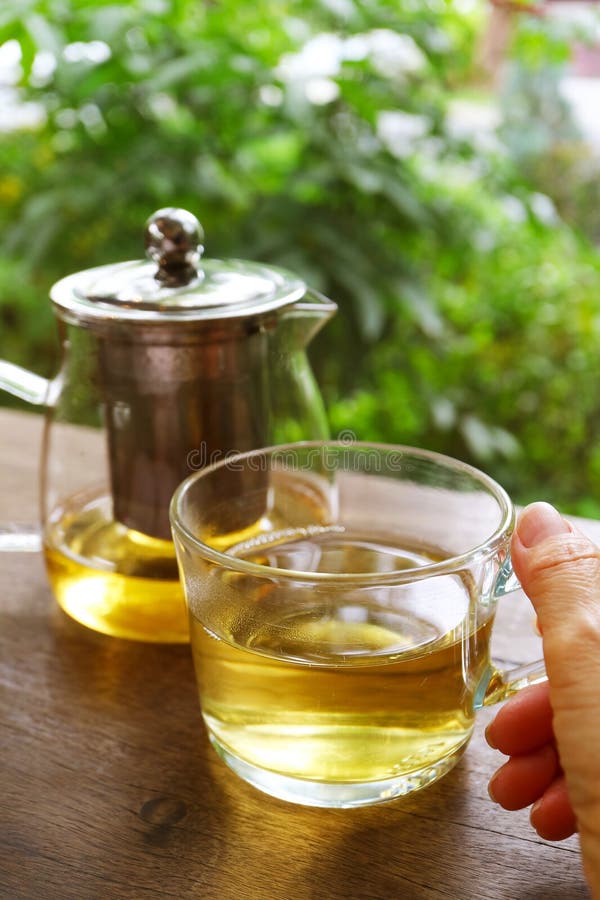 Hand Holding a Cup of Hot Tea with Tea Pot in the Backdrop Stock Image ...