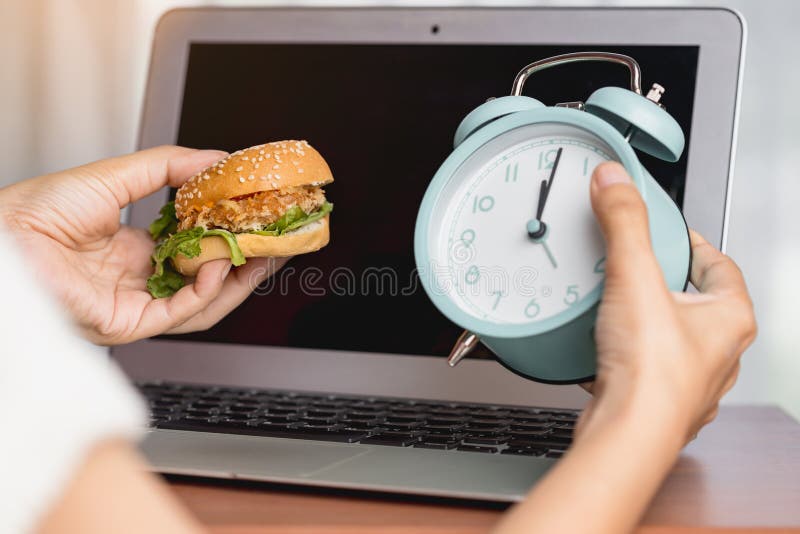 Hand Holding a Delicious Hamburger and Alarm Clock while Working Stock ...