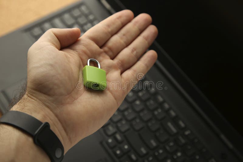 A Hand Holding a Green Padlock with a Laptop in Background. Cyber ...