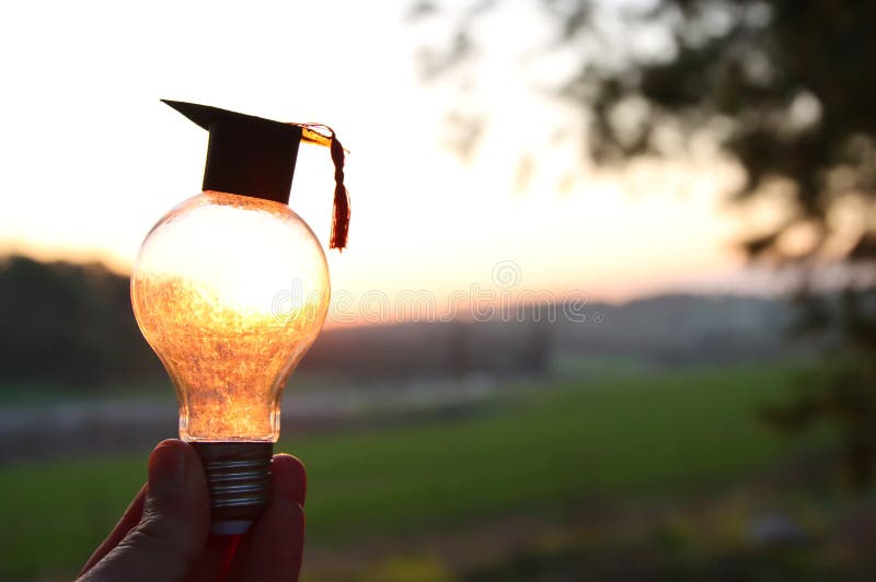 A Hand Holding a Light Bulb and Graduation Cap in Front of the Sun ...