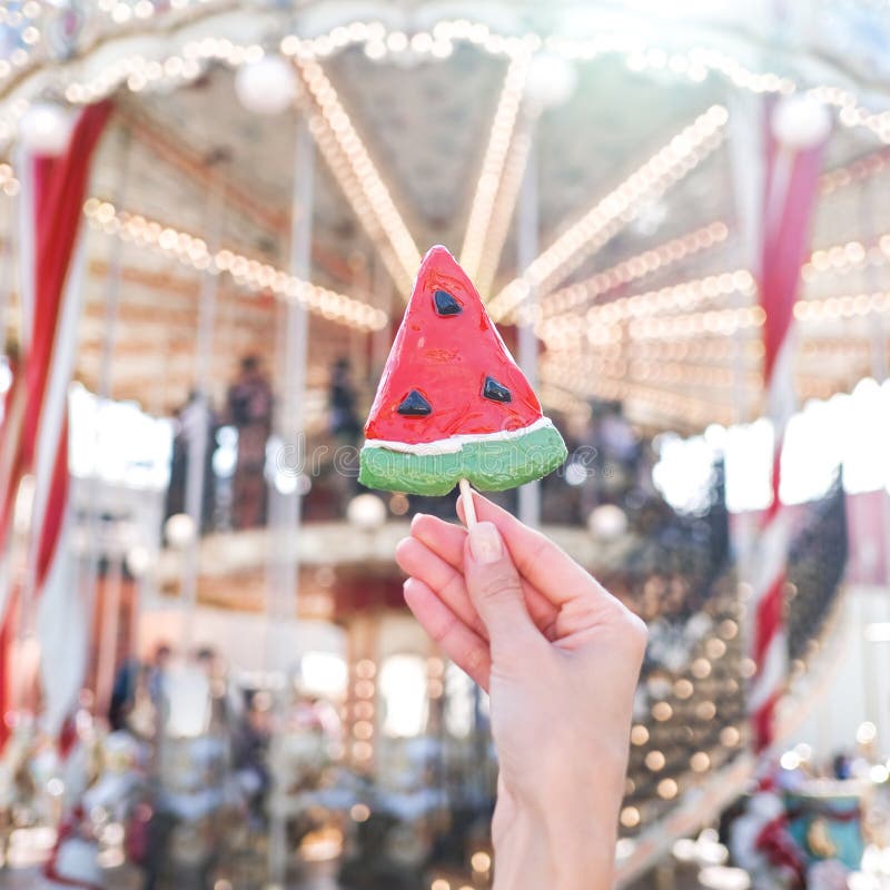 Hand Holding a Lollipop in Watermelon Shape, Carousel on Background ...