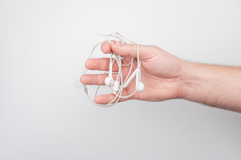 A Hand Holding a Pair of Tangled Earbuds Sits on a Light-colored ...