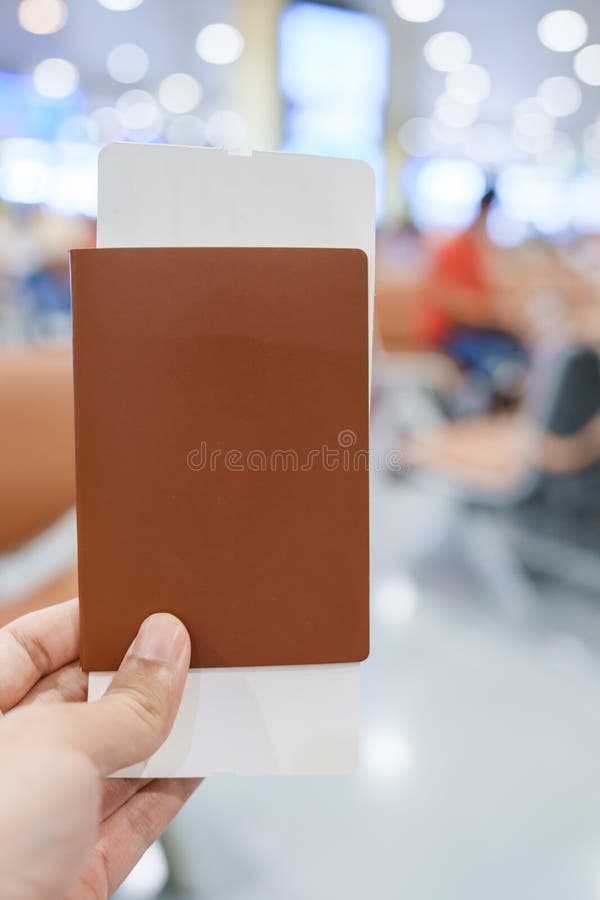 Hand Holding Passport And Boarding Pass Ticket In International Airport