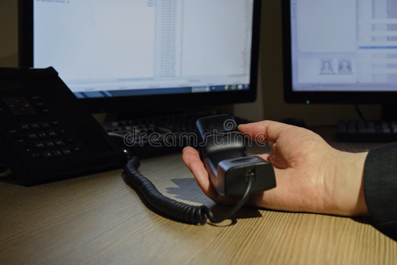 A Hand Holds a Landline Phone Handset on an Office Desk with Compute ...