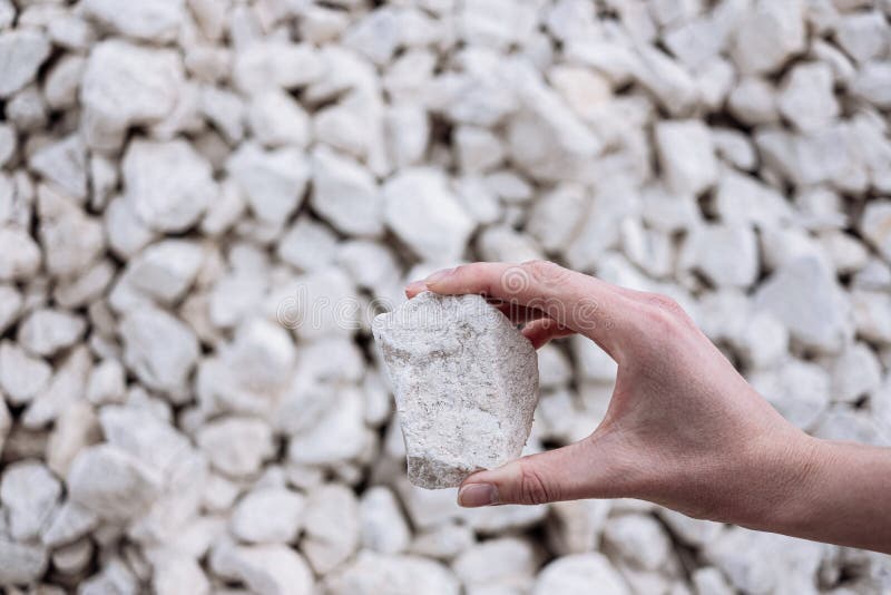 Hand Holds a White Chalkstone with a Lot of Stones on the Background ...