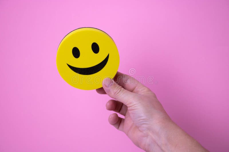The Hand Holds a Yellow Smiling Smiley Face on a Pink Background Stock ...
