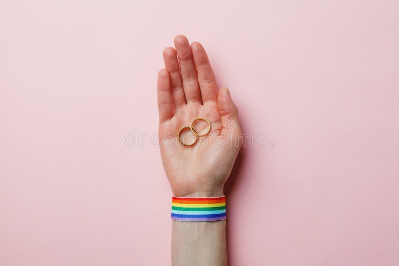 Hand With Lgbt Rainbow Ribbon Wristbands Holding Pair Of Golden Wedding