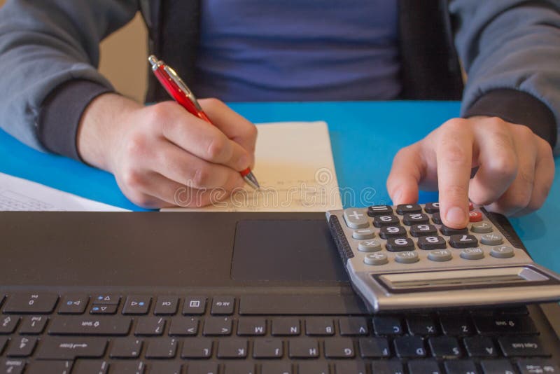 Hand with Pen, Calculator and Computer on Wooden Table. he is Using His ...