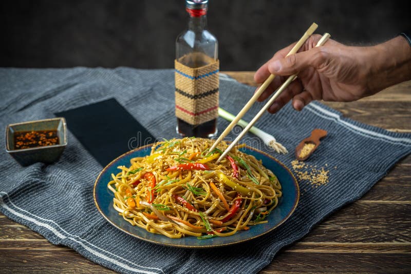 Hand Picking Chinese Noodles from the Blue Plate Over the Wooden Table ...