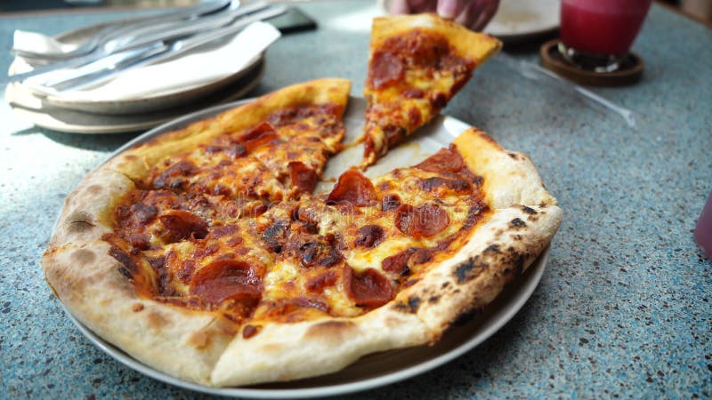 A Hand Picking Up the Sliced Pizza from a Plate on the Table Stock ...