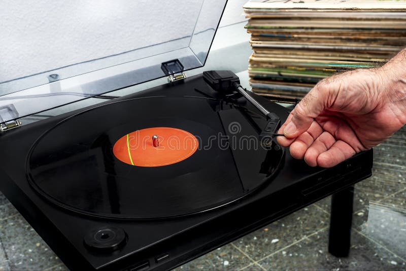 Hand Placing a Vinyl Record on a Record Player with a Stack of Vinyls ...