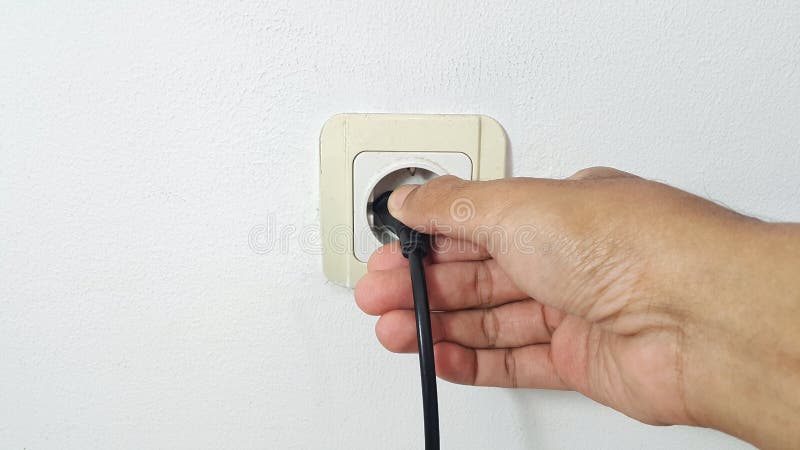 Hand Plugging in an Electric Cord into a White Plastic Socket on White ...