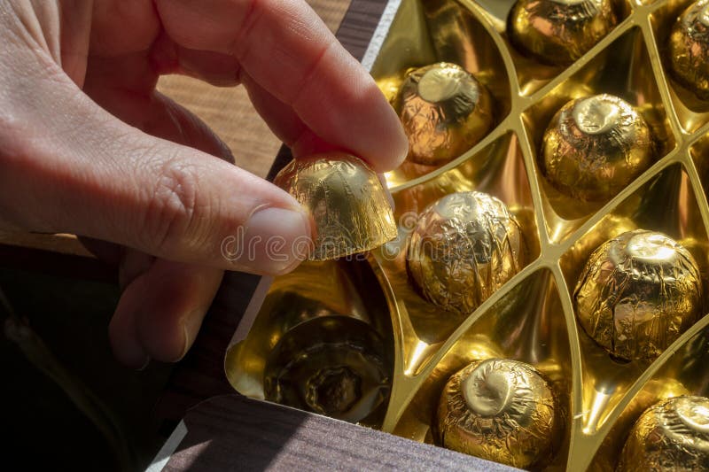 Hand Reaching for Chocolate in Golden Wrap in Box, Closeup View Stock ...