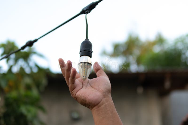 A Hand Reaching Up To an Exposed Light Bulb Hanging from a Wire Stock ...