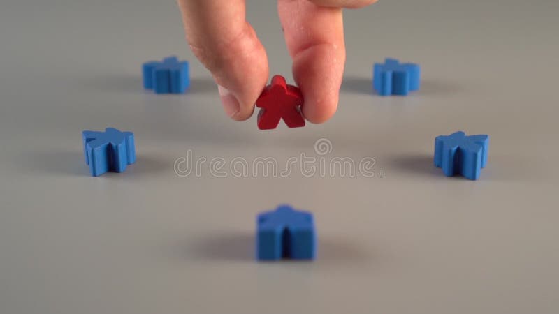 A Hand Sets a Red Figure Surrounded by Blue Figures on a Gray Surface ...