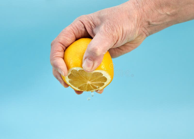 A Hand is Squeezing the Juice Out of Lemon, Isolated on Light Blue ...