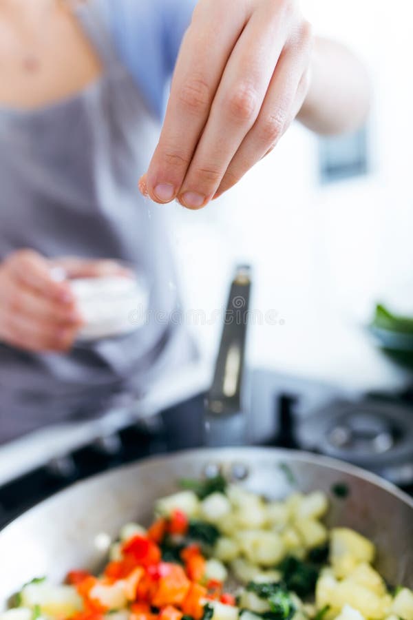 Hand of a Young Woman Adding Salt To Vegetables into the Pan. Stock ...