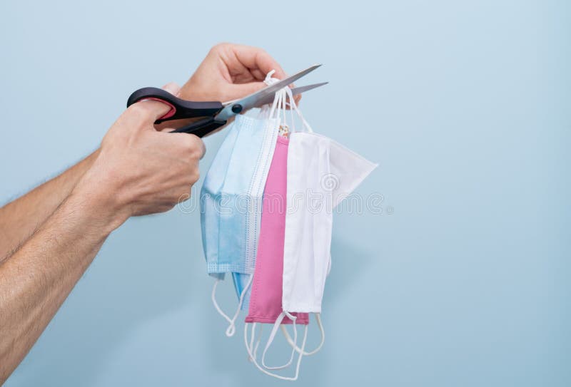 Hands Cutting a Group of Masks with Scissors on a Blue Background Stock ...