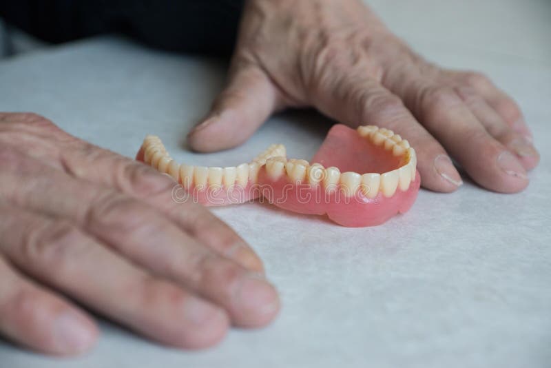 The Hands of an Elderly Man and False Teeth Dentures on the Table ...