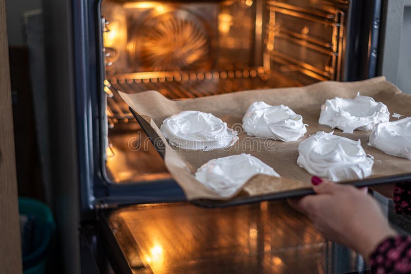 Hands Guiding a Batch of Fresh Meringues into the Warm Glow of an Oven ...