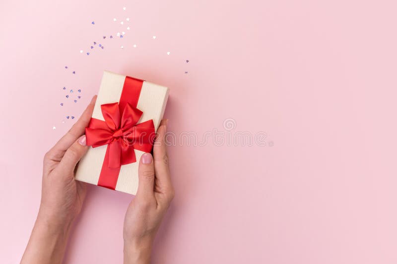 Hands Holding Gift Box with Red Bow on Pink Background with Confetti ...