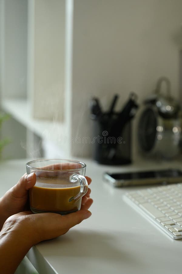 Hands Holding Hot Coffee in a Glass Mug beside a Modern Computer Stock ...