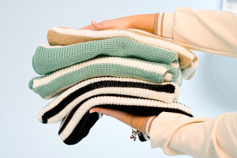 In the Hands of a Man is a Stack of Knitted Clothes of Different Colors ...