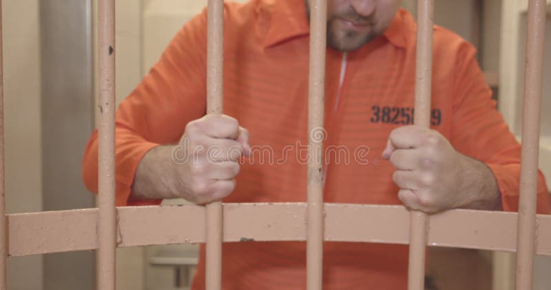 Hands of Prisoner in Orange Uniform Hold the Bars of the Prison Cell ...