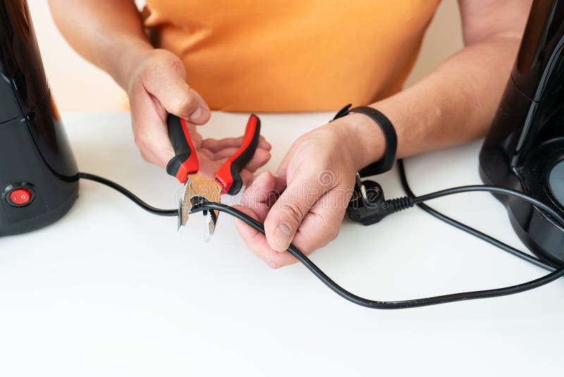 Hands Using Pliers To Cut a Black Cable on a White Background ...