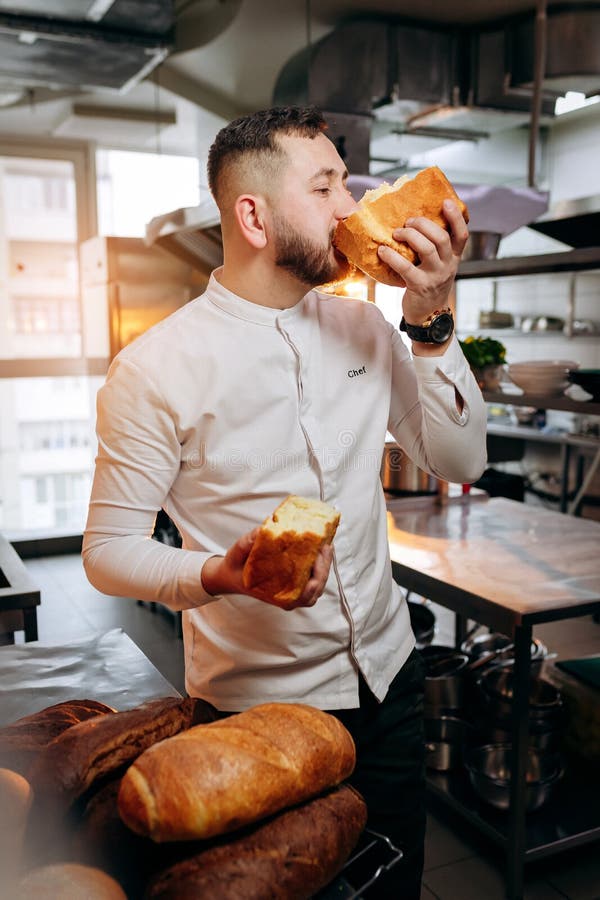 Handsome Baker in Uniform Biting Freshly Baked Bread at the Bakery ...