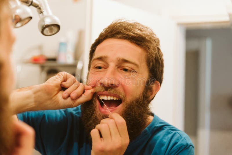 Handsome Bearded Man Looking at Mirror while Using Dental Floss in ... Handsome Bearded Man Looking at Mirror while Using Dental Floss in ...