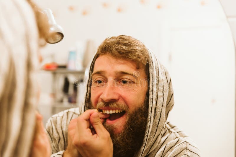 Handsome Bearded Man Looking at Mirror while Using Dental Floss in ... Handsome Bearded Man Looking at Mirror while Using Dental Floss in ...