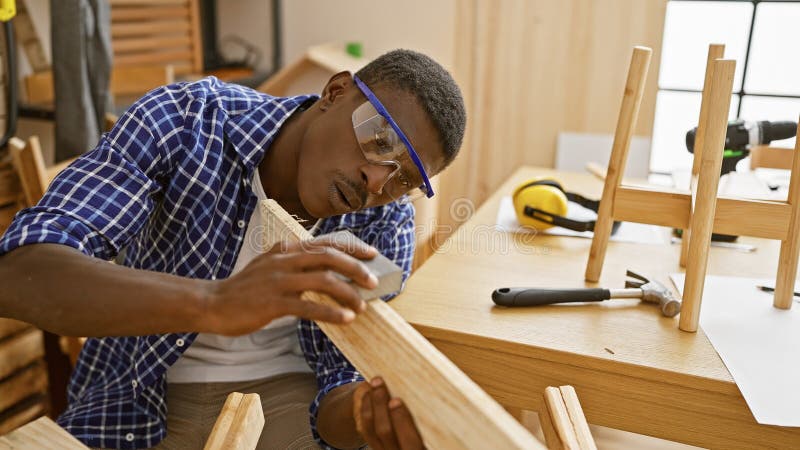Handsome Black Man Sanding Wood Diligently in a Well-equipped Carpentry ...