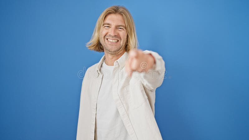 Handsome Blond Man Pointing and Smiling Against a Solid Blue Background ...