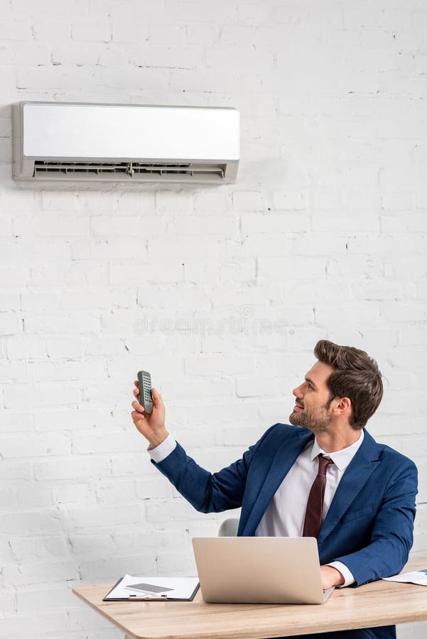 Businessman Holding Remote Control while Sitting at Workplace Under Air ...