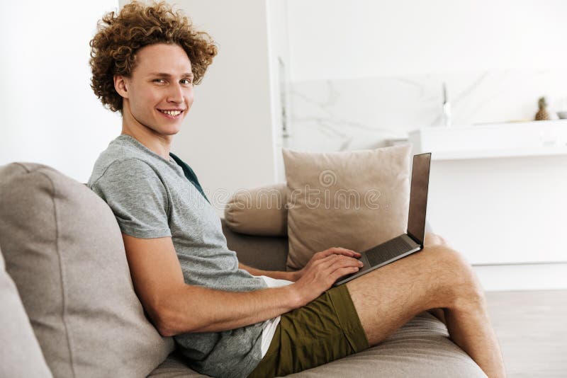 Handsome Cheerful Man Sitting at Sofa Using Laptop Computer. Stock ...
