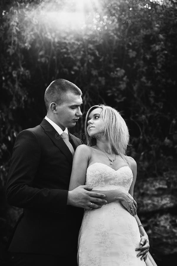 Handsome Groom Hugging Blonde Bride From Behind In Forest Bandw Stock