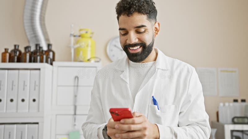 Handsome Hispanic Male Lab Technician in White Coat Using Smartphone in ...