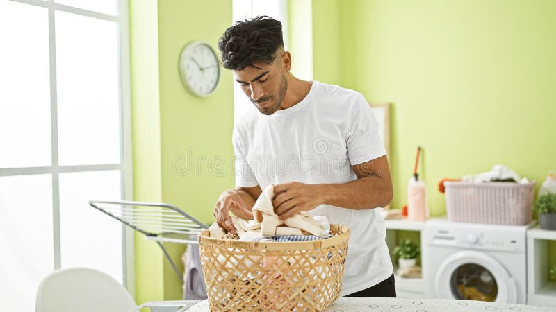 Handsome Hispanic Man Folding Laundry in a Tidy, Bright Green Room ...