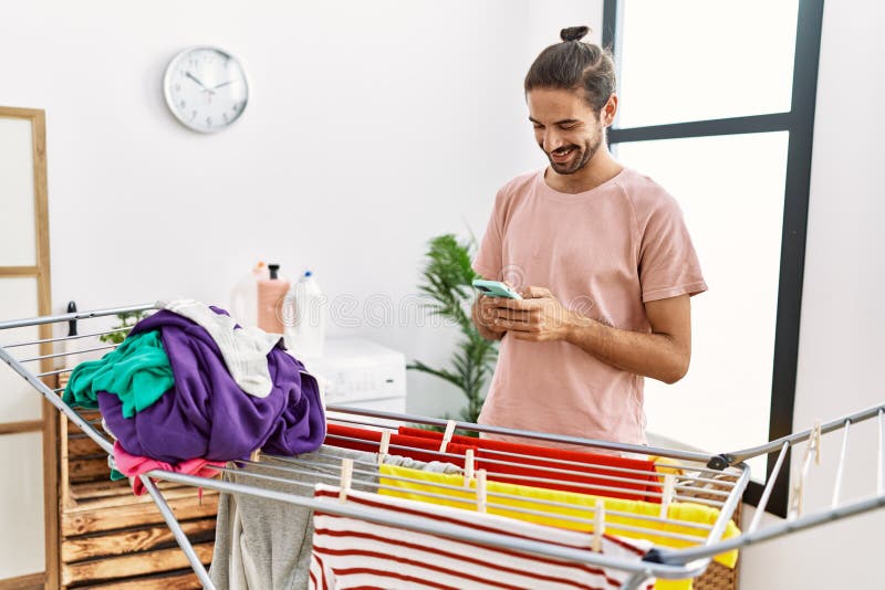 Handsome Hispanic Man Hanging Laundry Using Smartphone at Laundry Room ...