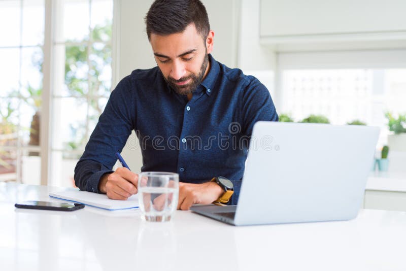 Handsome Hispanic Man Working Using Computer and Writing on a Paper ...