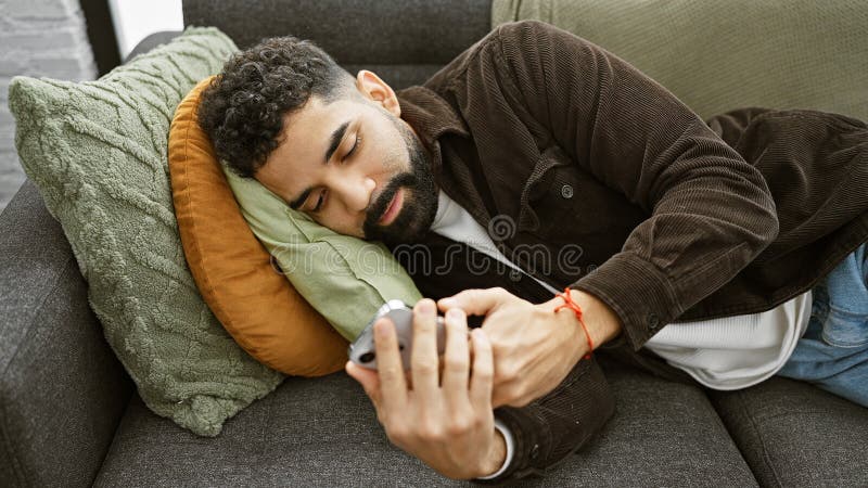 Handsome Man with Beard Lying on a Couch at Home, Holding a Smartphone ...